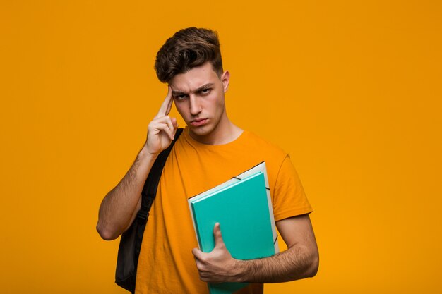 Hombre joven estudiante sosteniendo libros tratando de escuchar un ... Hombre joven estudiante sosteniendo libros tratando de escuchar un ...