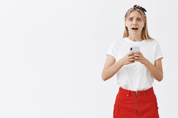Garota atraente moderna usando telefone celular e parecendo ansiosa e ... Garota atraente moderna usando telefone celular e parecendo ansiosa e ...