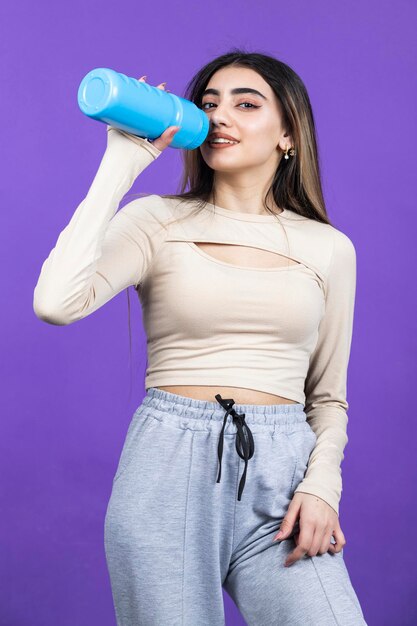 Jovem tentando beber água uma jovem em forma fica em fundo roxo foto de ... Jovem tentando beber água uma jovem em forma fica em fundo roxo foto de ...