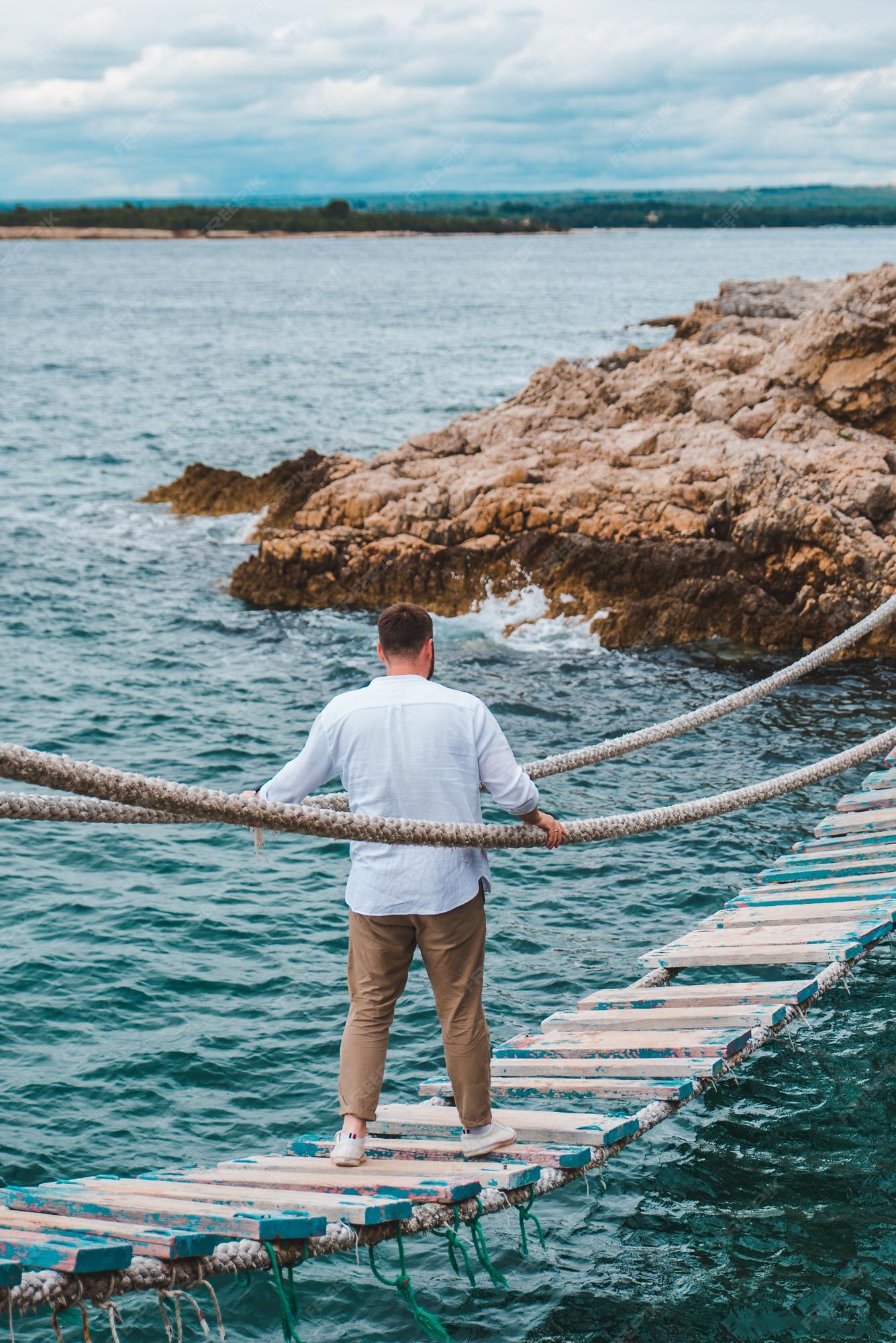 Homem andando pela ponte suspensa cruzar a baía do mar | Foto Premium Homem andando pela ponte suspensa cruzar a baía do mar | Foto Premium