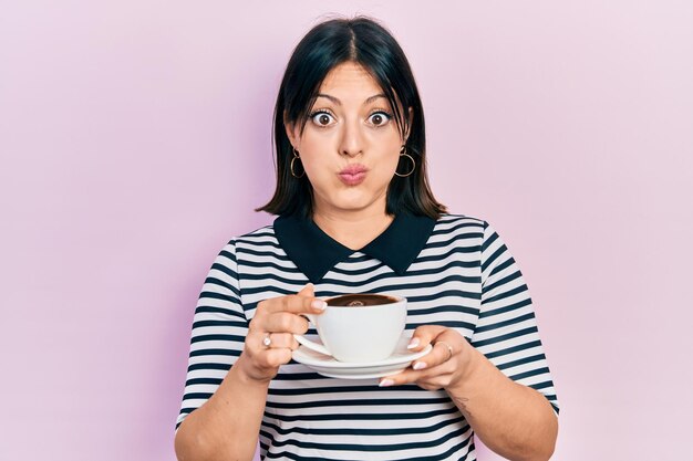 Junge hispanische frau, die eine tasse kaffee trinkt und die wangen ... Junge hispanische frau, die eine tasse kaffee trinkt und die wangen ...