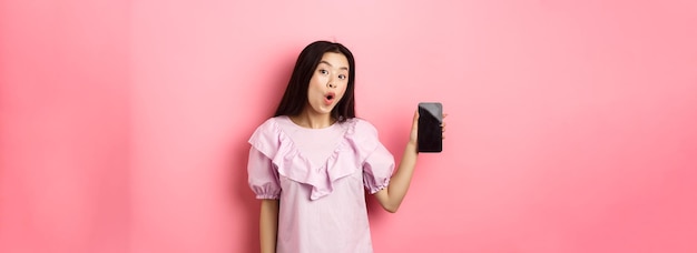 온라인 쇼핑에 흥분한 아시아 여성은 텅 빈 스마트폰 화면을 보여주고 캘리포니아에 놀란 표정을 짓고 있습니다 무료 사진