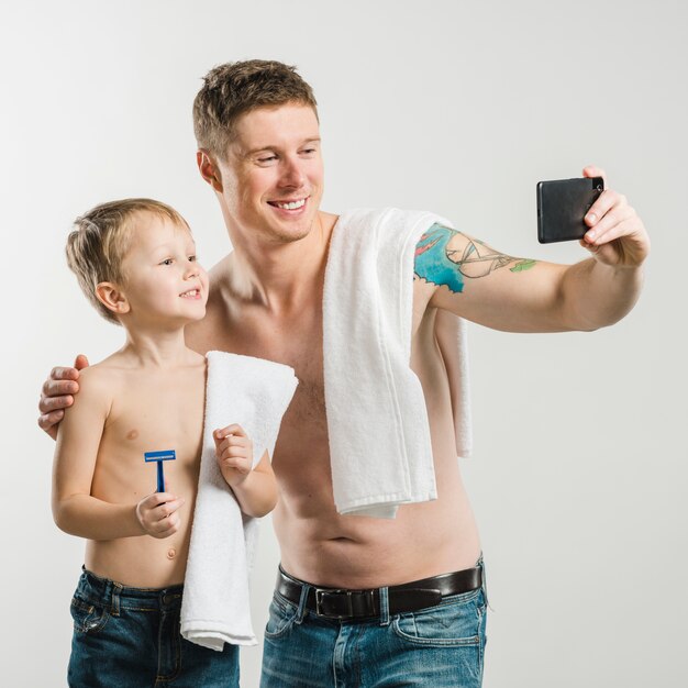 Free Photo Shirtless Father And Son With White Towels Over Their Shoulders Taking Selfie On