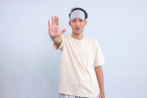 スリーピングマスクをかぶったアジア人男性が手を挙げストップジェスチャーを示しています プレミアム写真