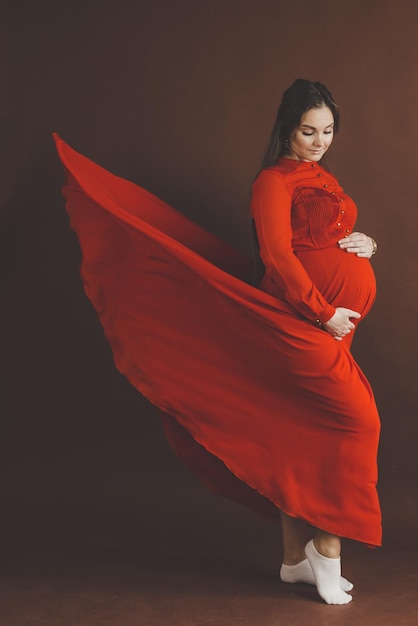 Premium Photo Pregnant Woman In Red Flying Dress Holding Her Belly