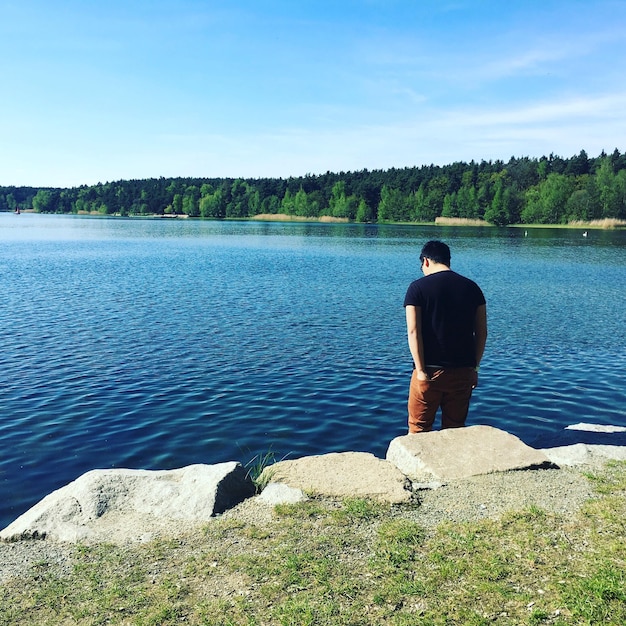 Premium Photo Rear View Of Man Standing At Lakeshore Against Blue Sky
